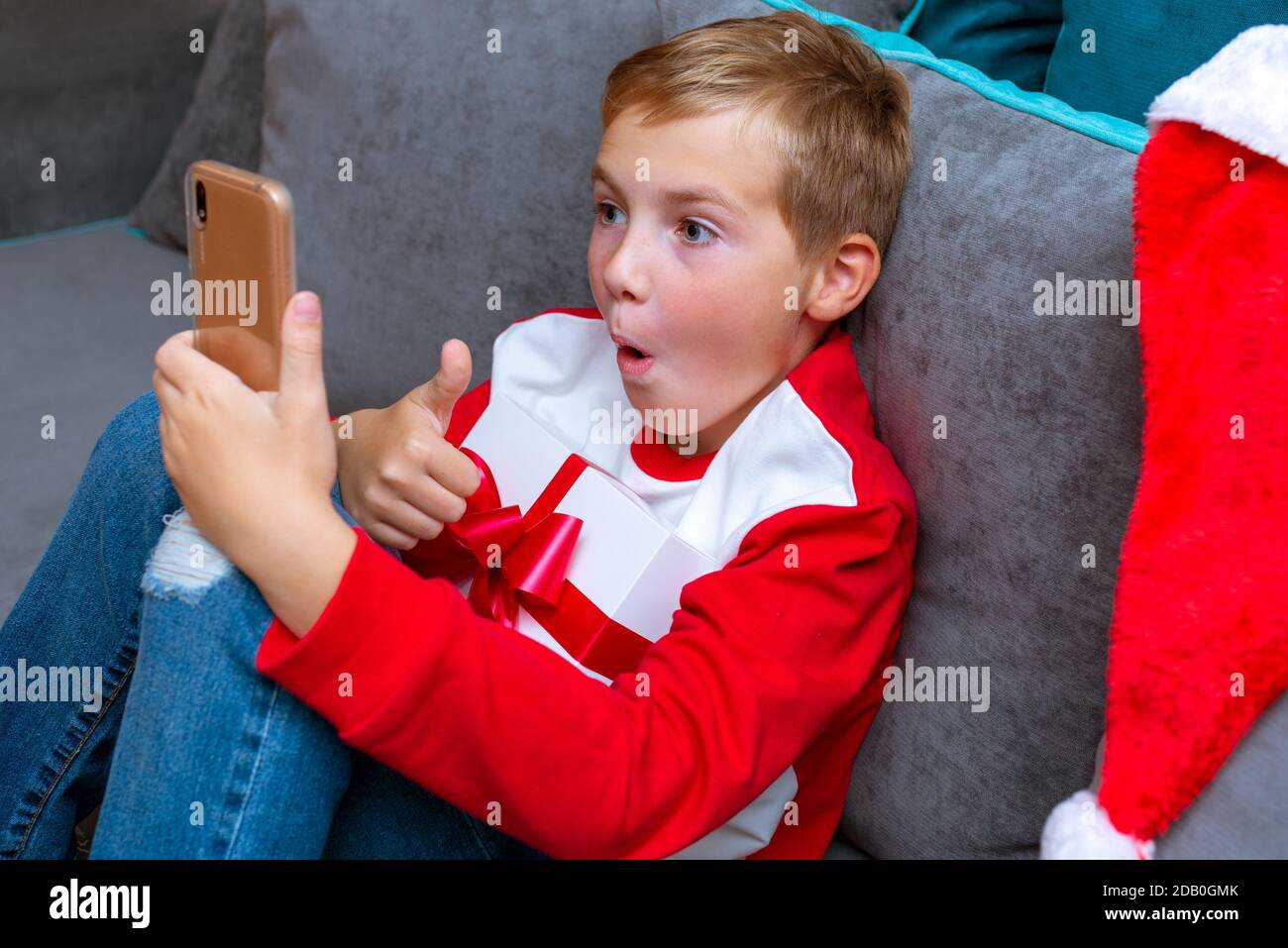 Surprised Handsome kid boy in Santa Claus hat looks at smartphone ...