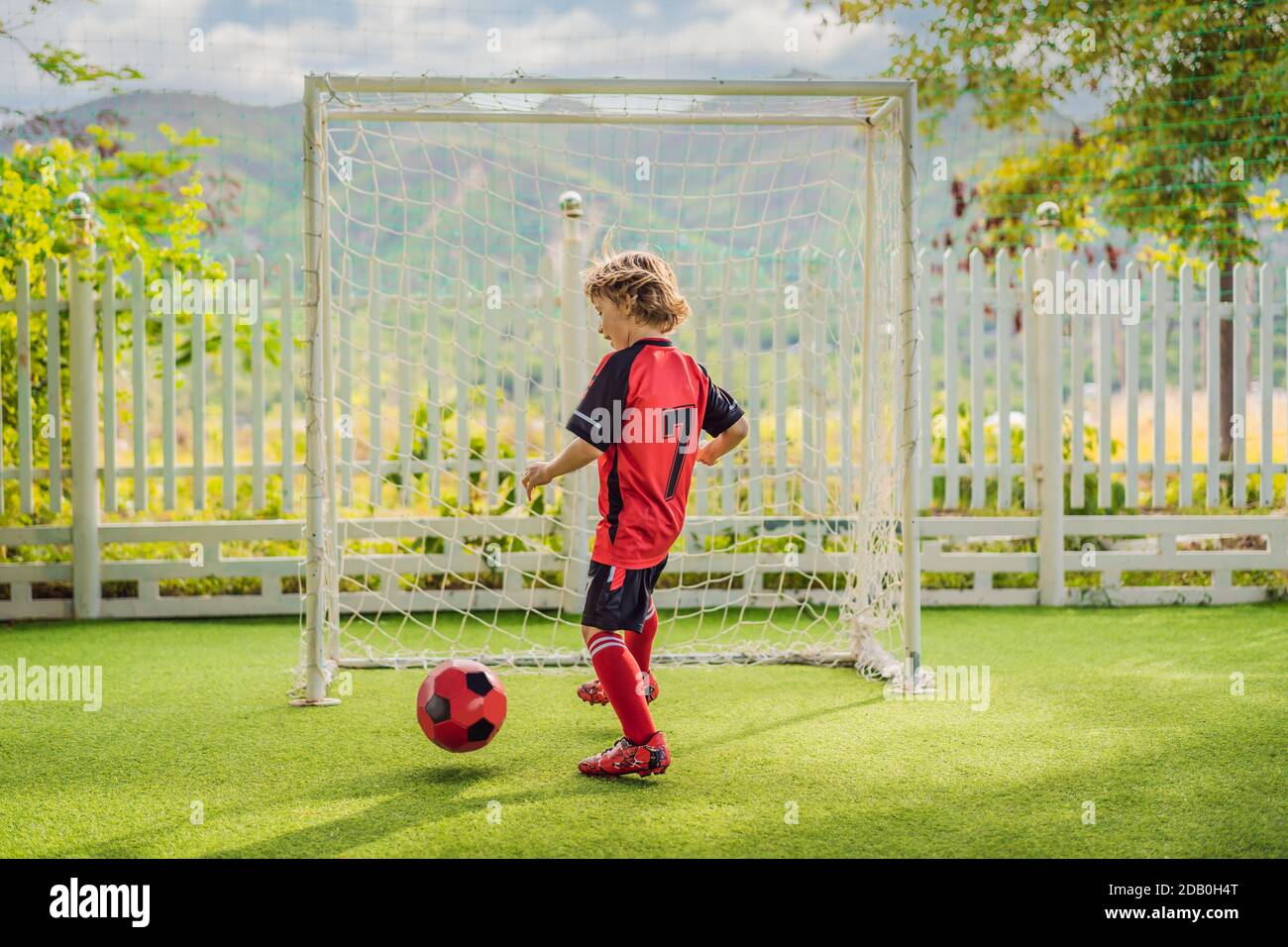 Little cute kid boy in red football uniform playing soccer, football on ...