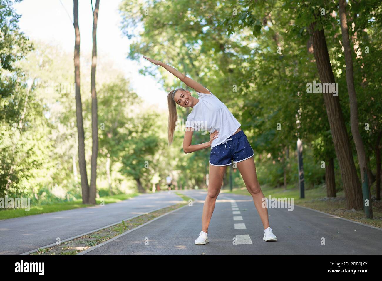 Woman runner stretching arms before exercising summer park morning ...