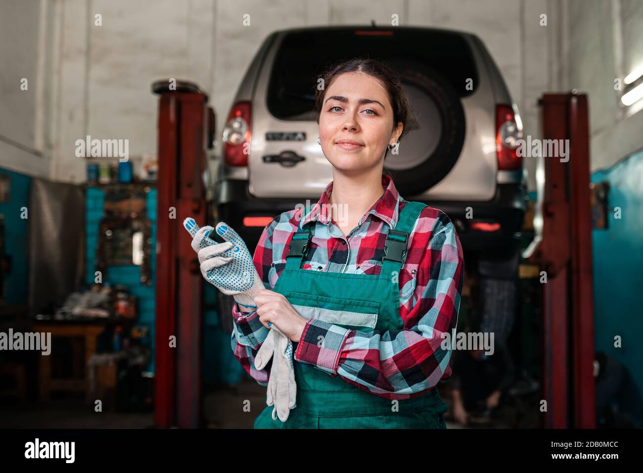 Portrait of a young female mechanic in uniform, wearing work gloves. In ...