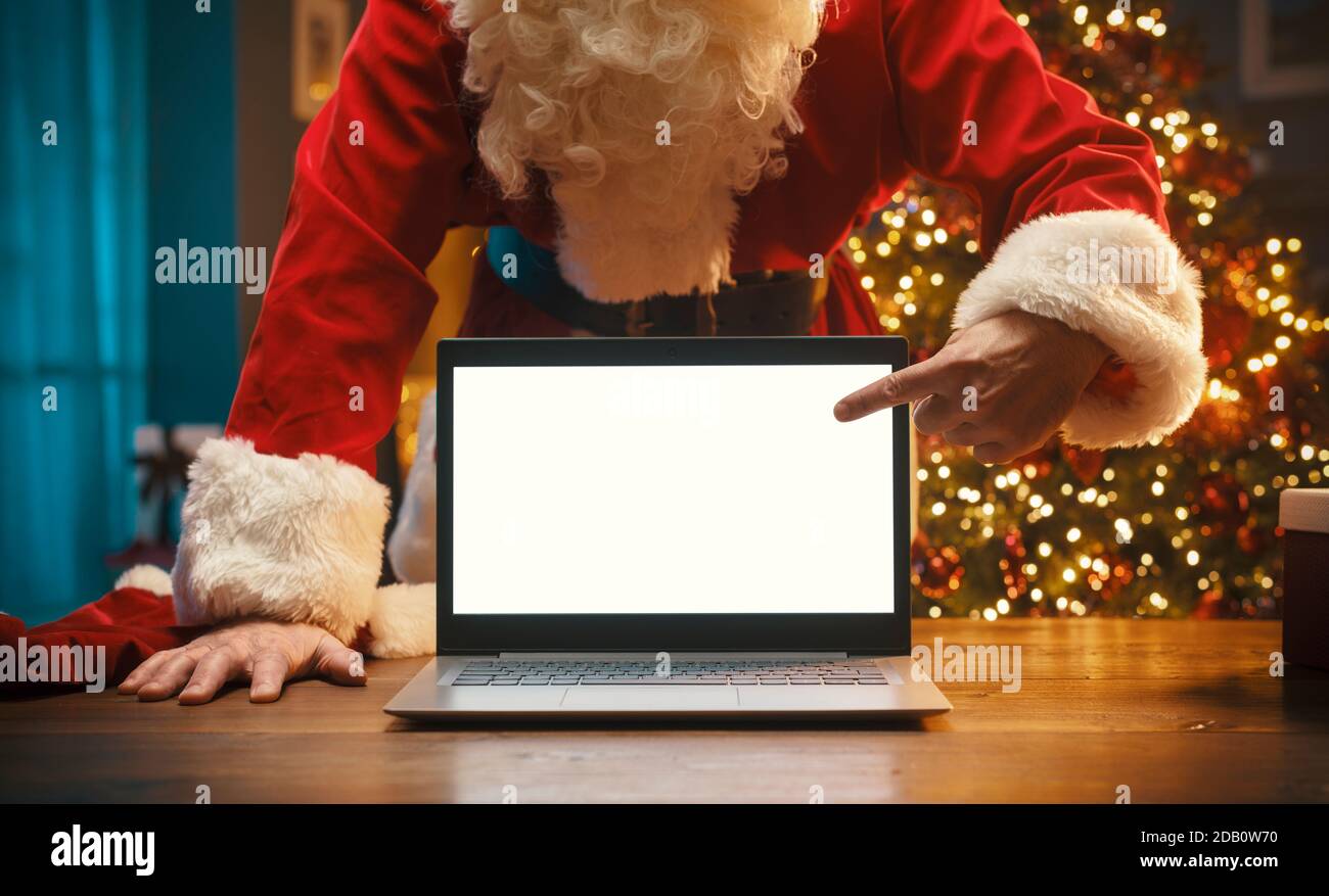 Santa Claus standing behind a desk and pointing at the laptop screen ...