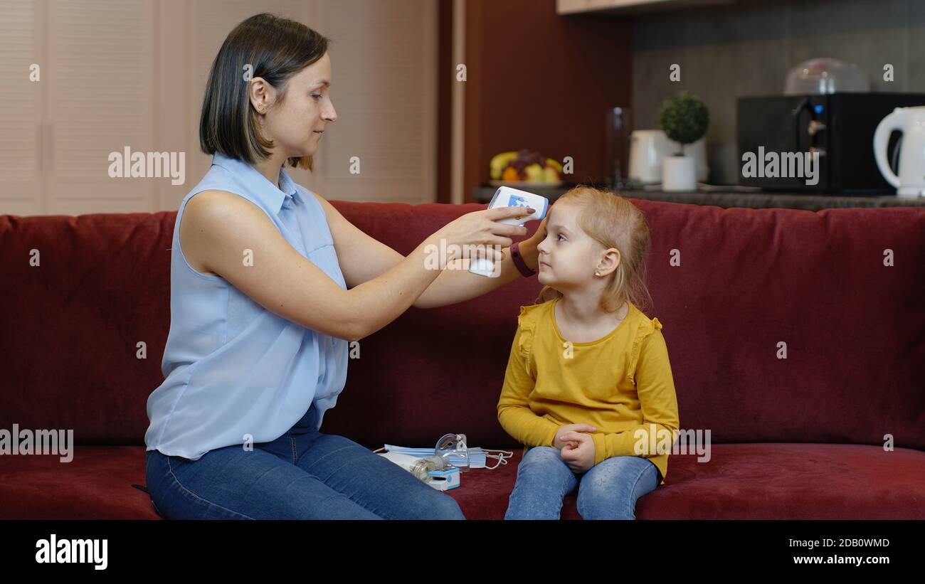 Mother measures temperature with contactless digital thermometer of her little sick daughter ...