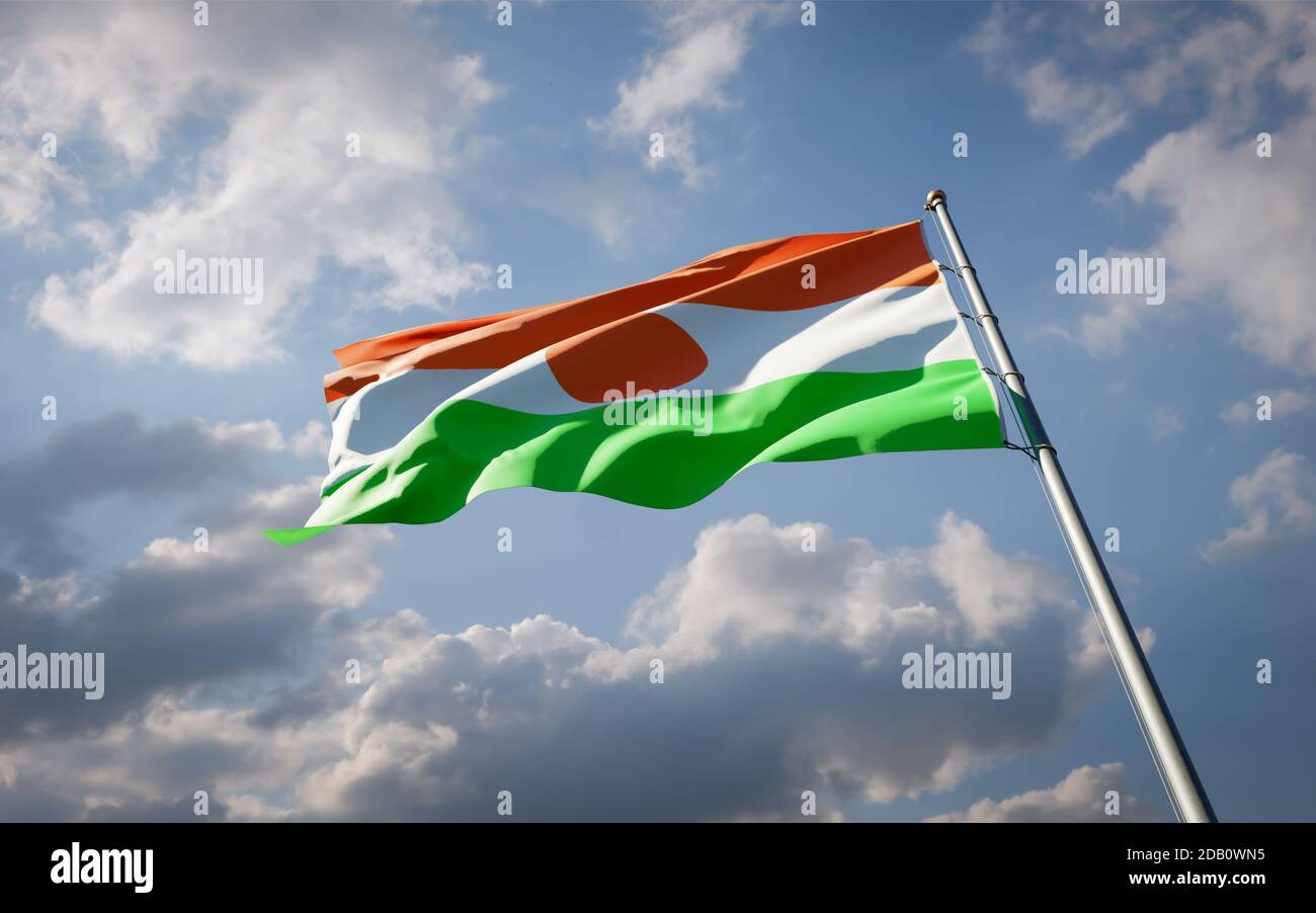 Beautiful national state flag of Niger fluttering at sky background ...