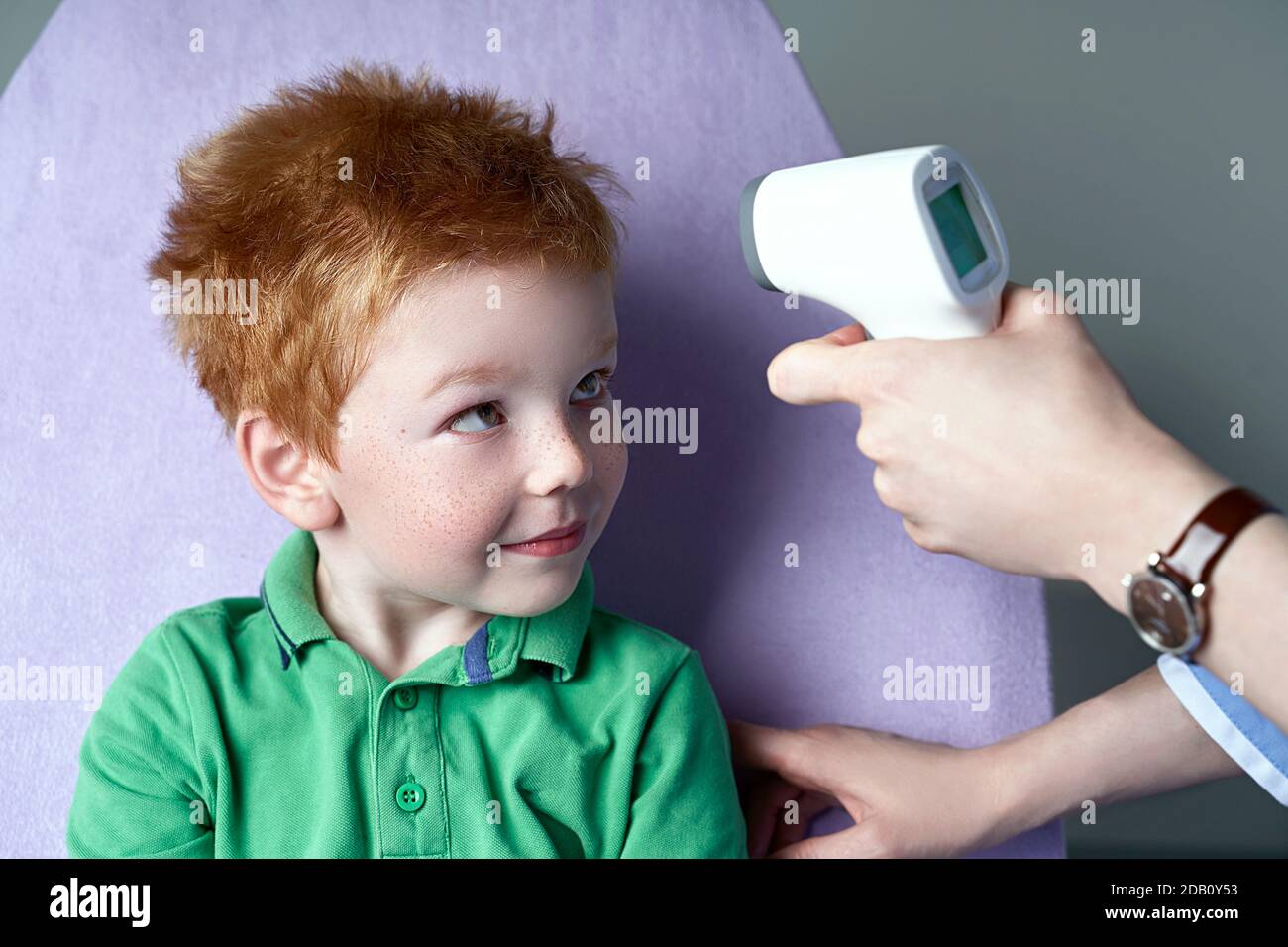 Doctor measures temperature of a cute red haired freckled little boy ...