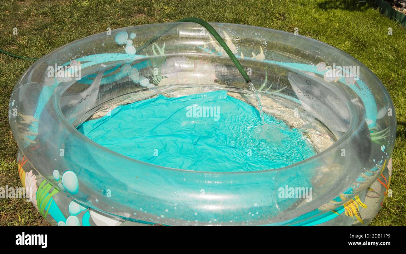 A plastic pool is filled with water from a rubber hose on a summer day ...