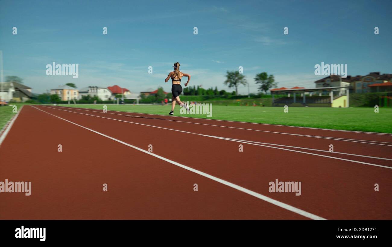 Athletic muscular woman running fast on racetrack at stadium, back view ...