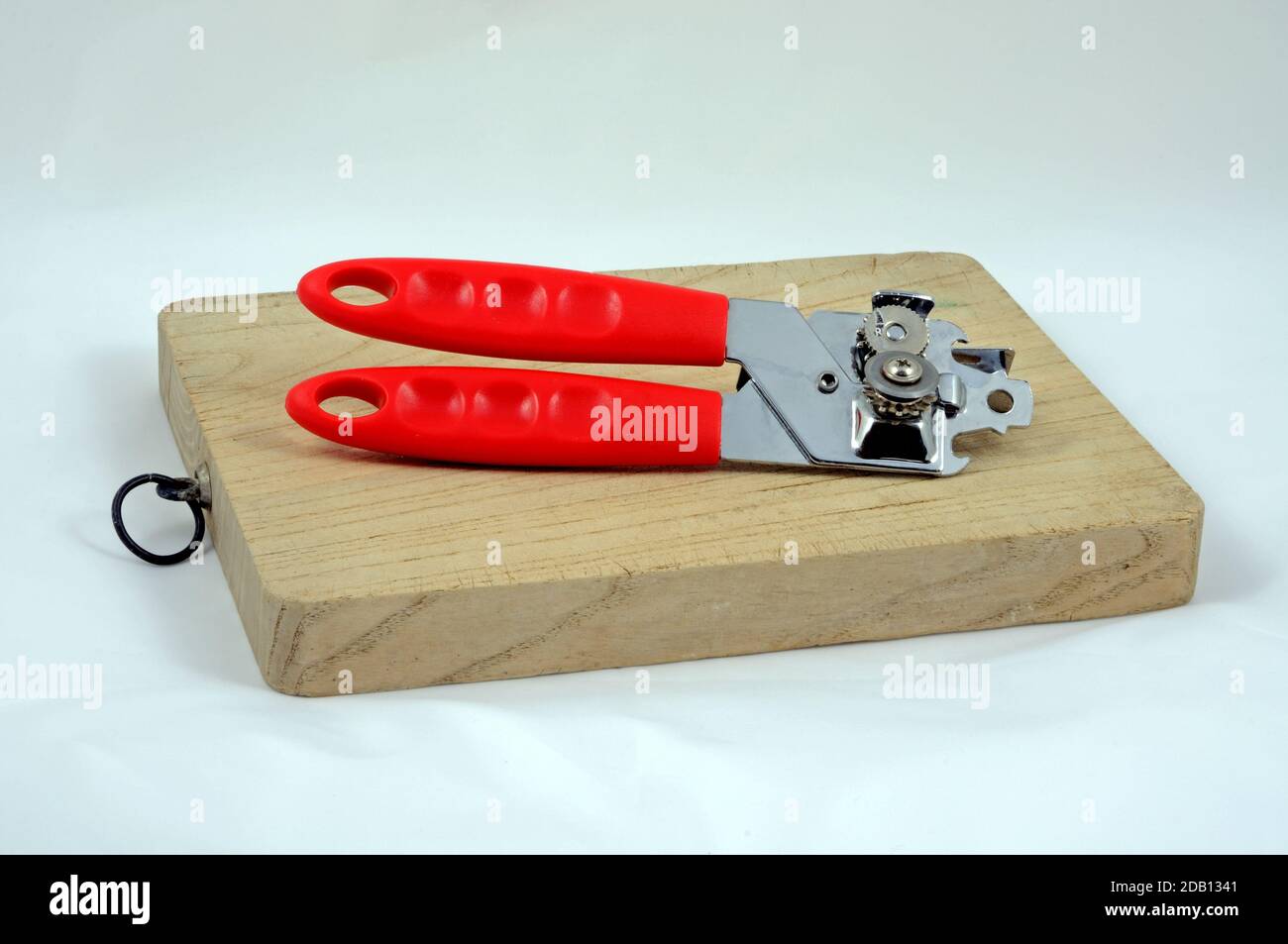 Hand operated Can opener with red grip on a small woden chopping board ...