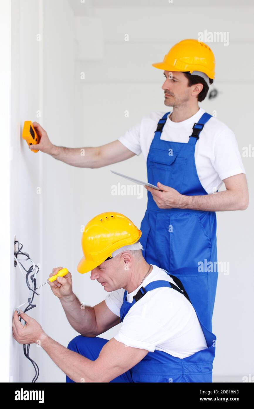 Electrician working with cable inside house, foreman measuring wall ...