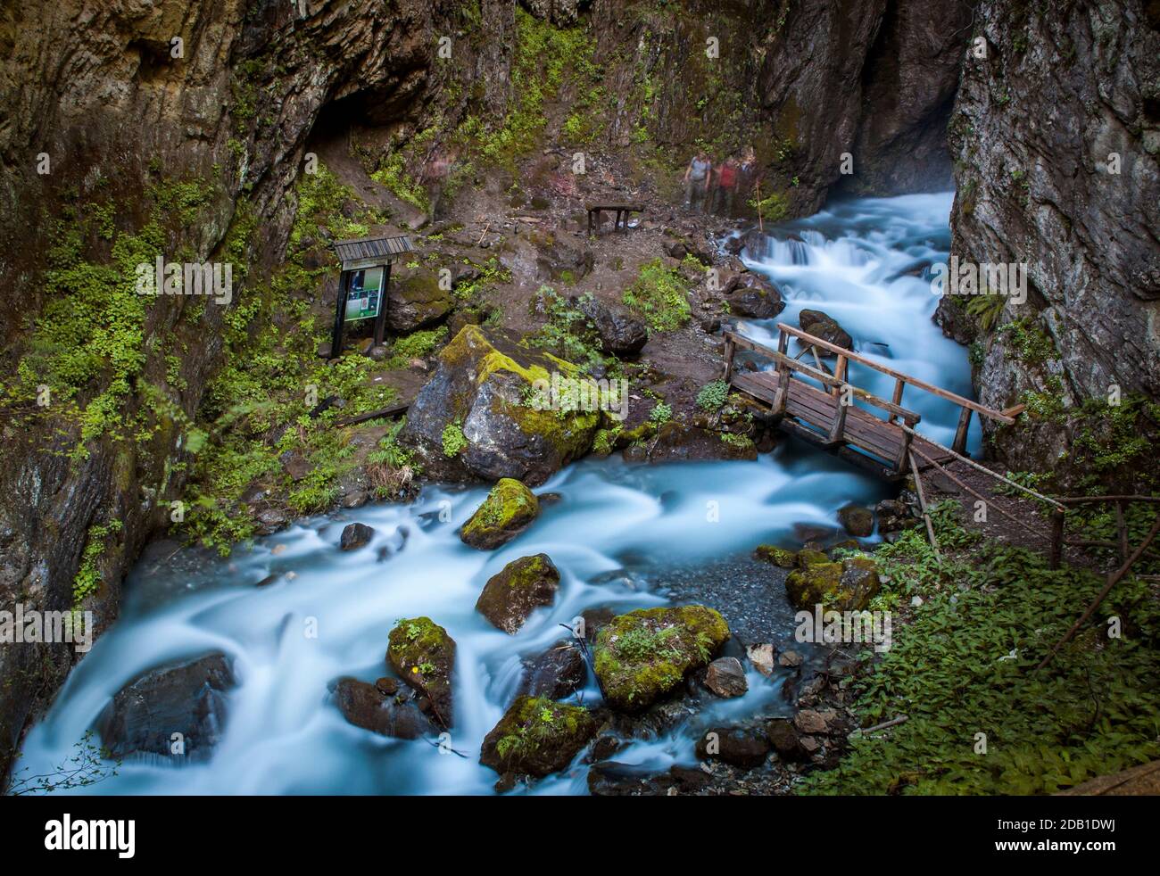 A stream flows through the rocks high in the mountain. A wooden bridge ...