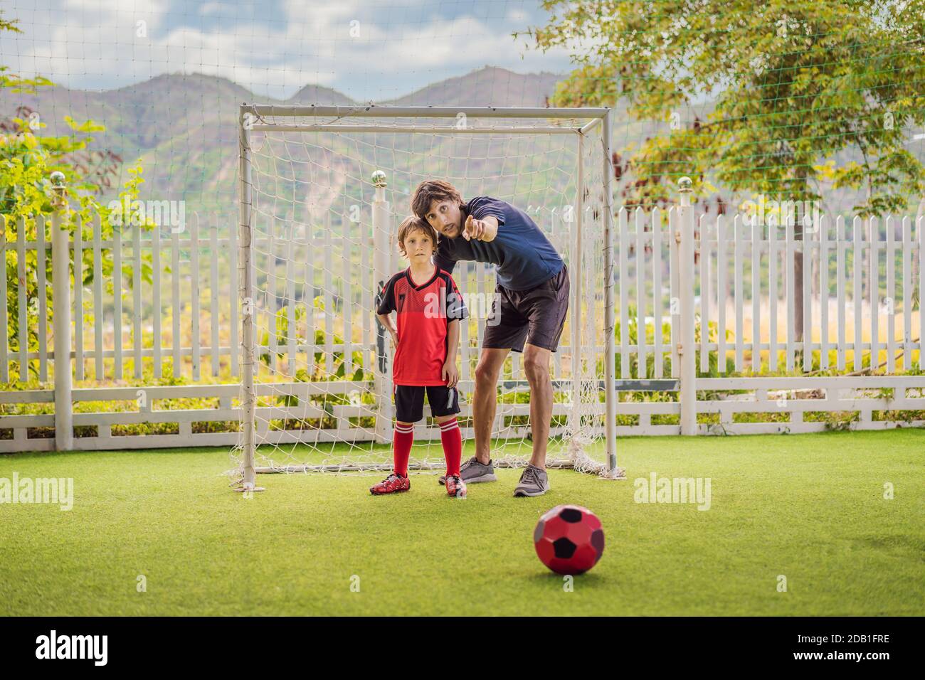 Little cute kid boy in red football uniform and his trainer or father ...