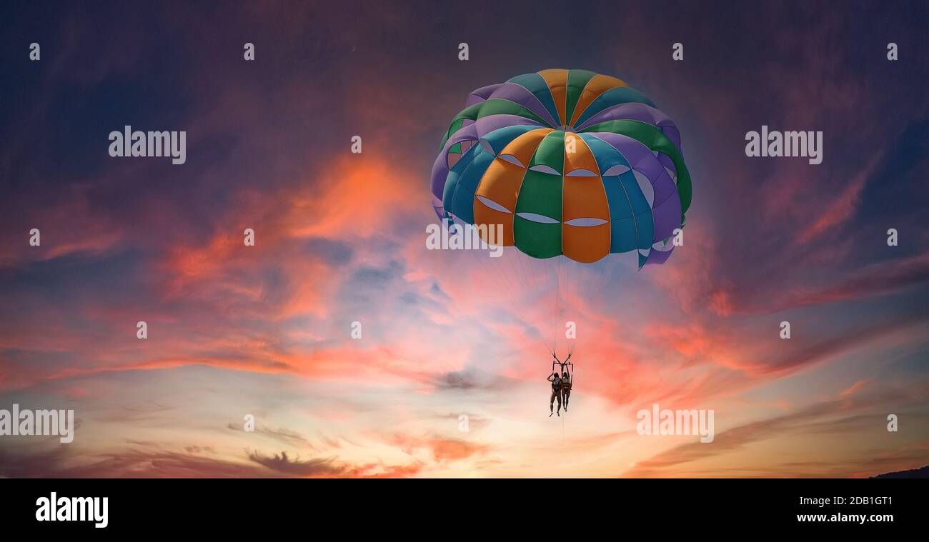 Two people enjoy parasailing flight during sunset bright pink and ...