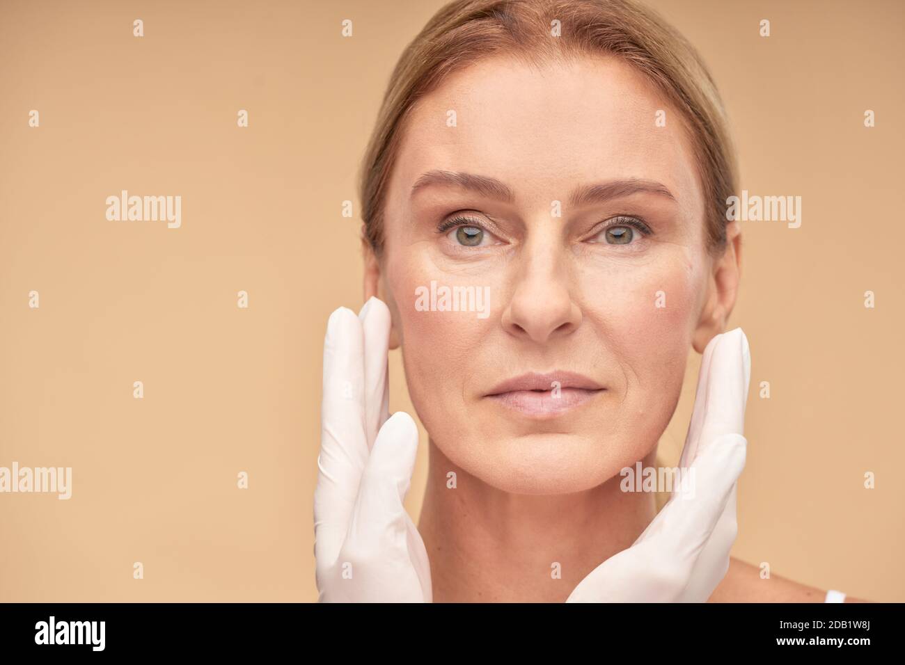 Cosmetology and skincare concept. Beautician hands in white gloves checking female face skin ...