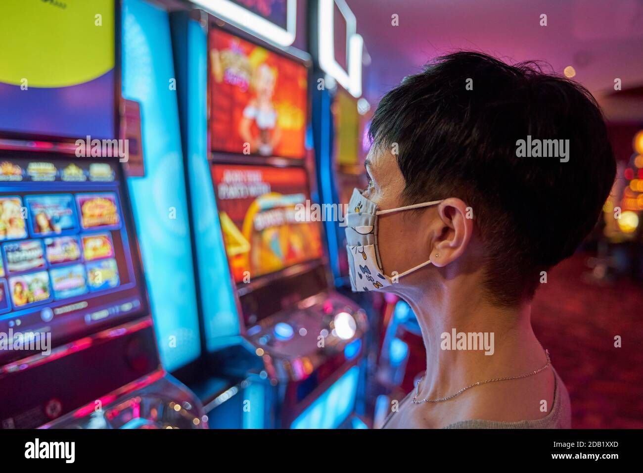 Black short haired female with Covid mask on playing the slot machines ...