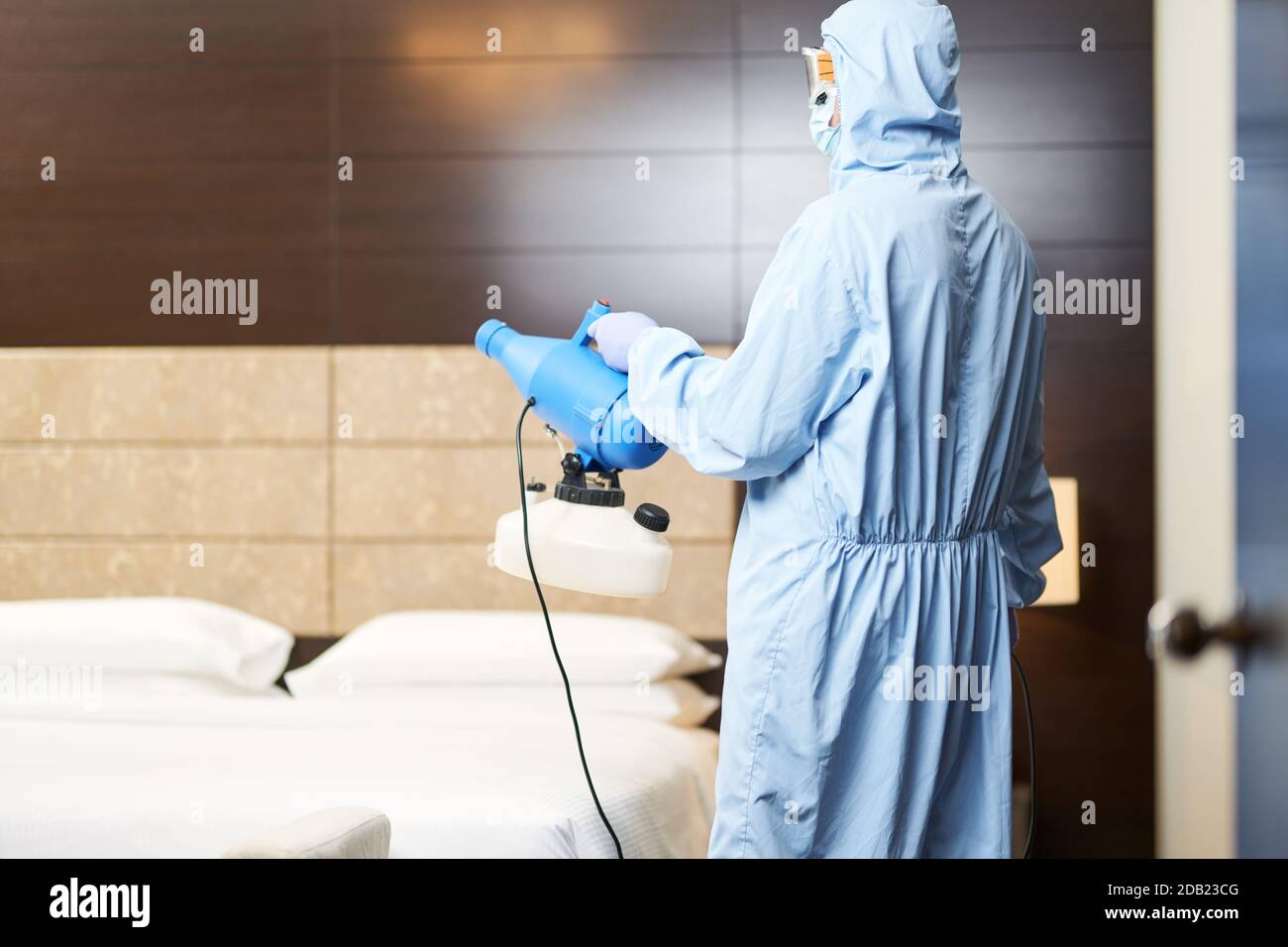 Back view of man in protective suit and face mask spraying for ...