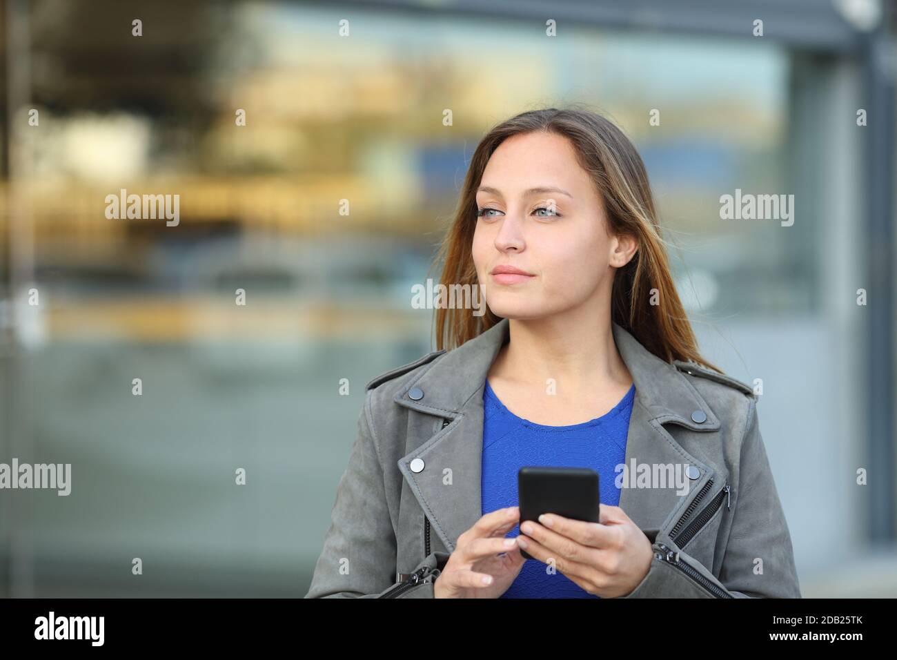 Confident entrepreneur holding mobile phone looks at side in the street Stock Photo - Alamy