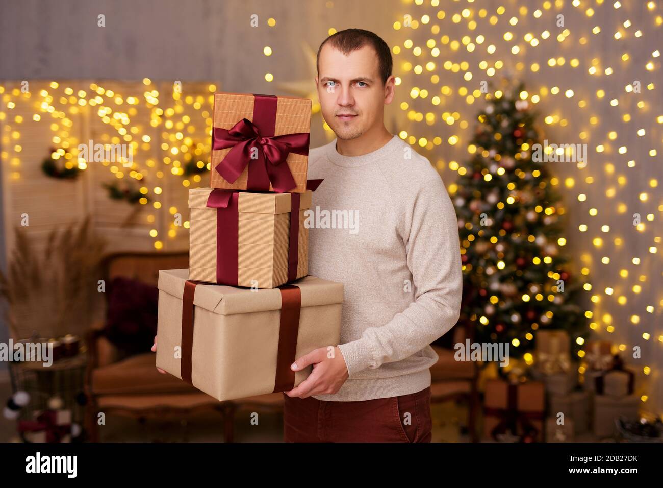 young handsome man holding heap of gift boxes over christmas background ...