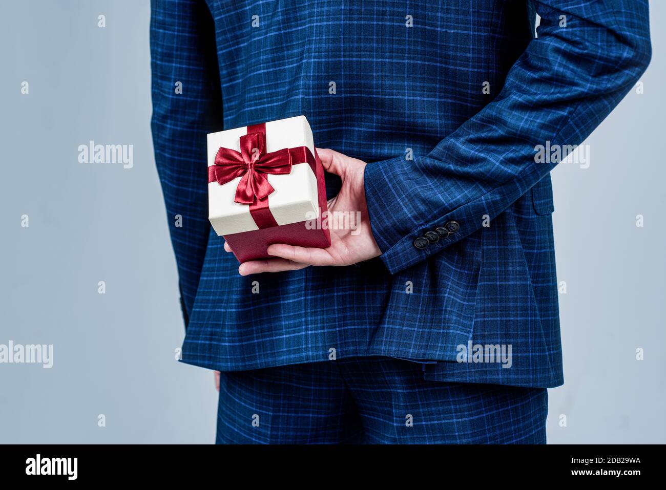 Gift box tied with red ribbon bow held in male hand behind back in ...