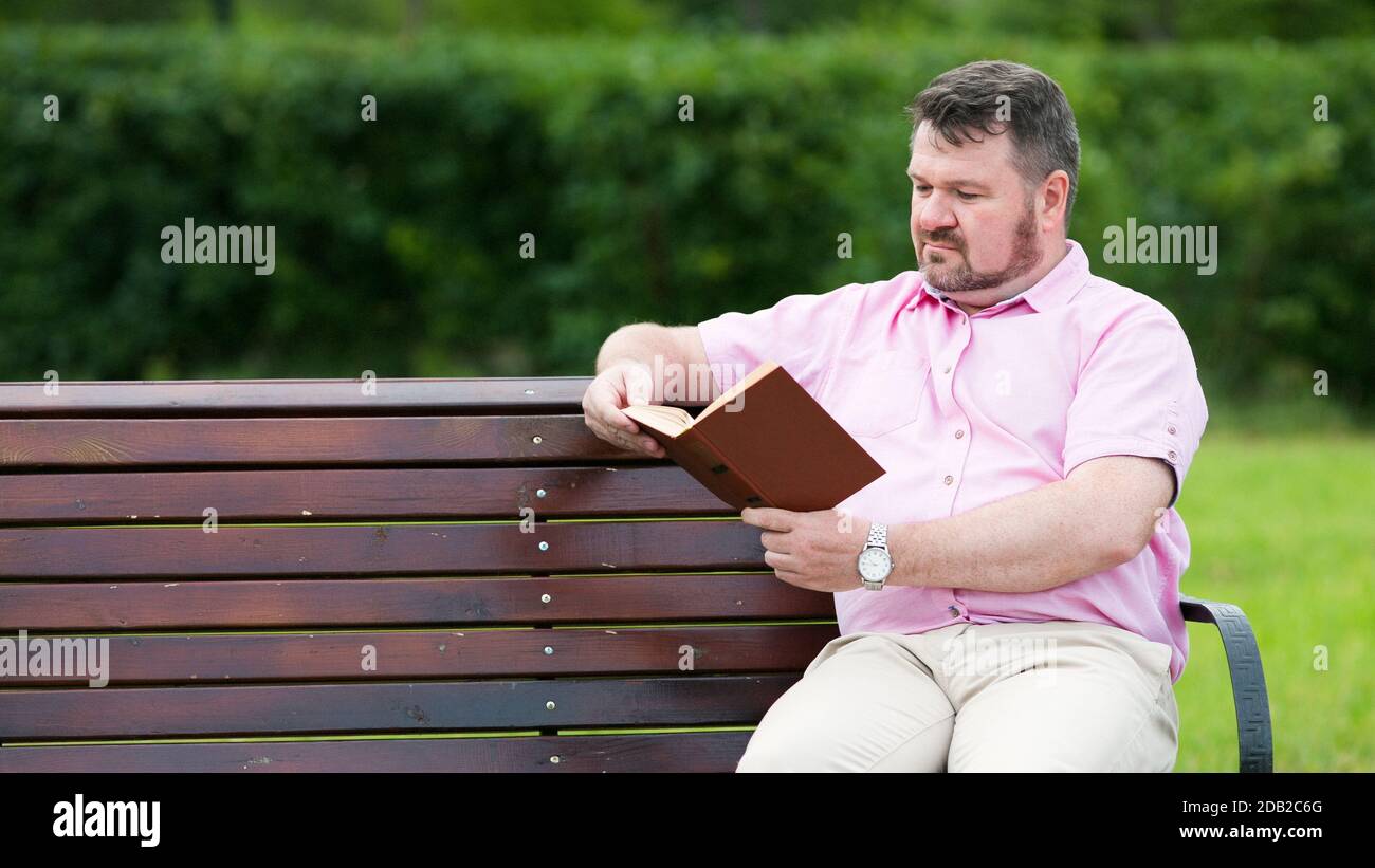 A plump man is reading a book on the bench Copy space Stock Photo - Alamy