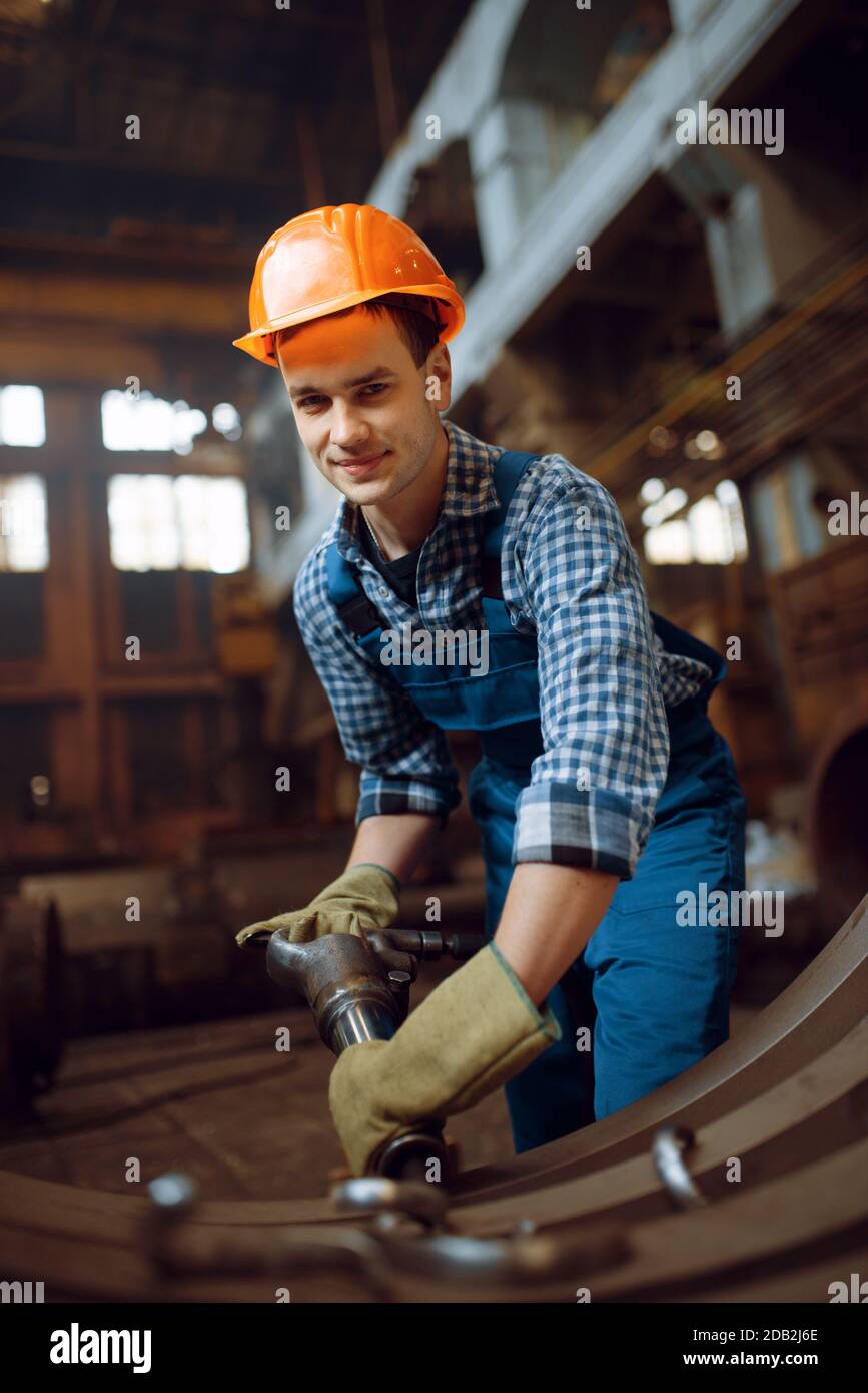 Male worker in uniform and helmet removes scale from metal workpieces ...