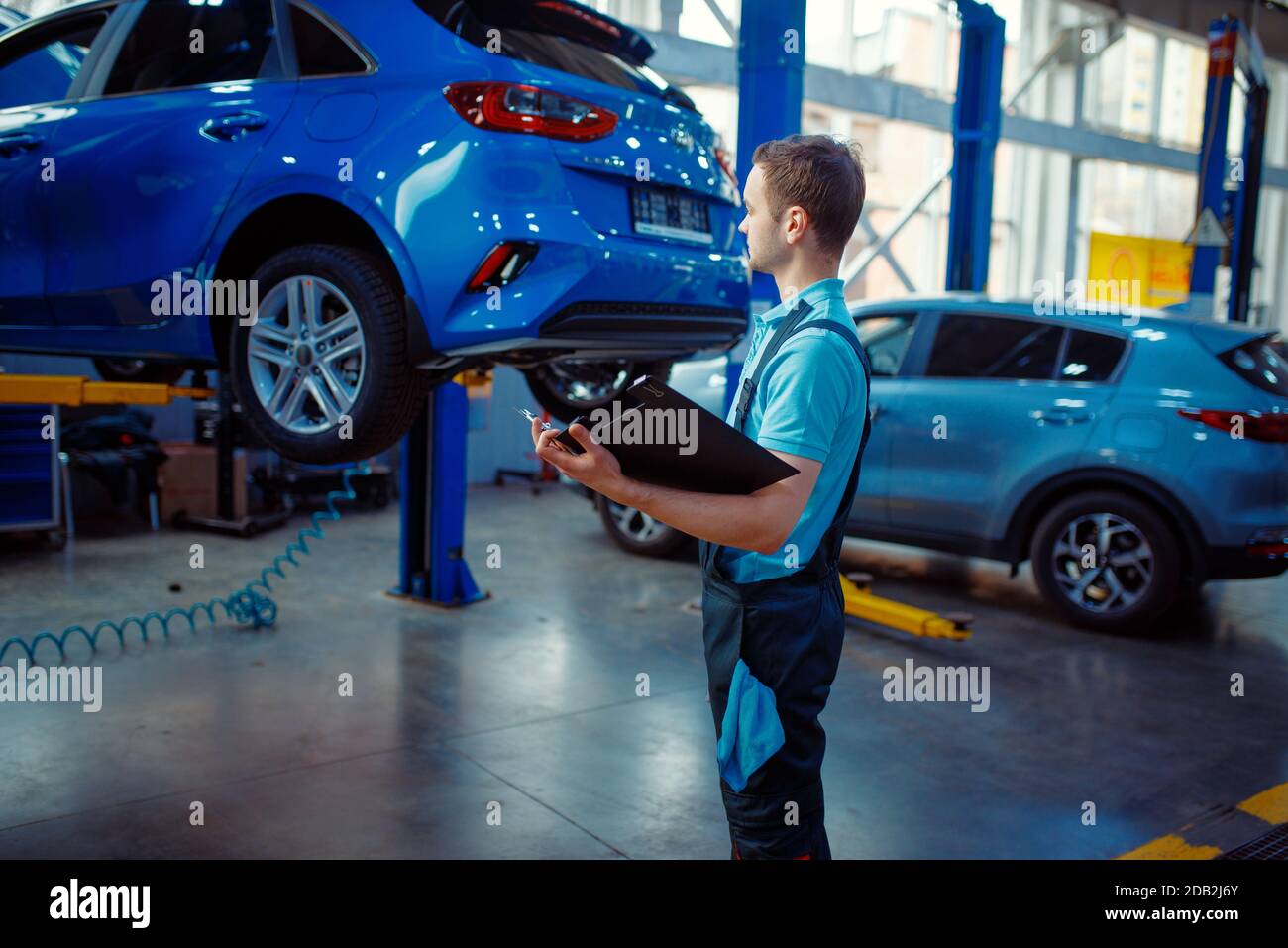 Repairman with a checklist stands at vehicle on lift, car service ...