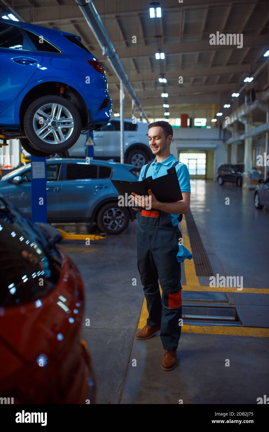 Worker with a checklist stands at vehicle with opened hood, car service ...