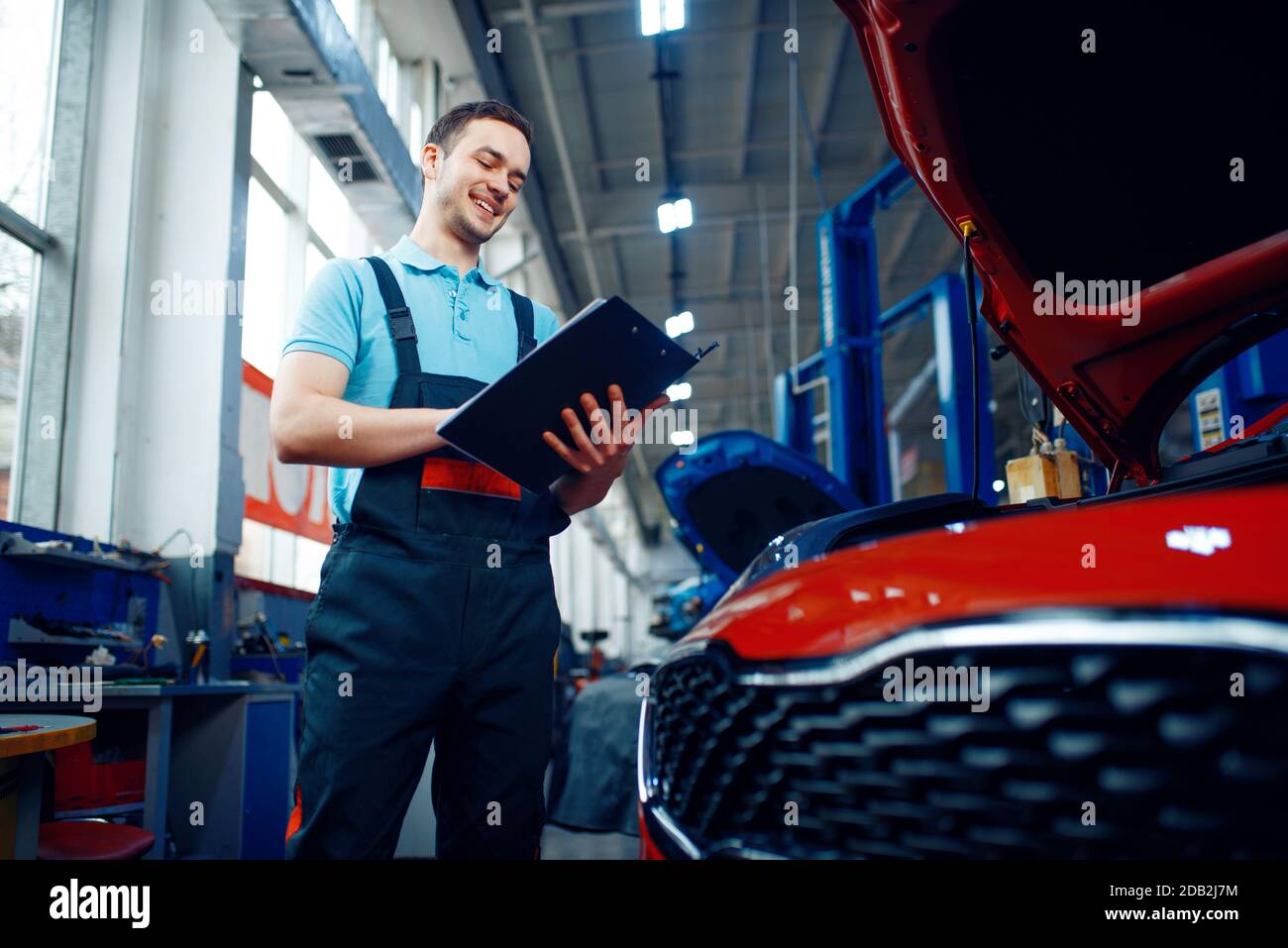 Worker with a checklist stands at vehicle with opened hood, car service ...