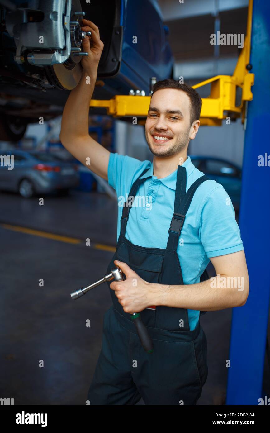 Repairman in uniform repairing vehicle on lift, car service station ...
