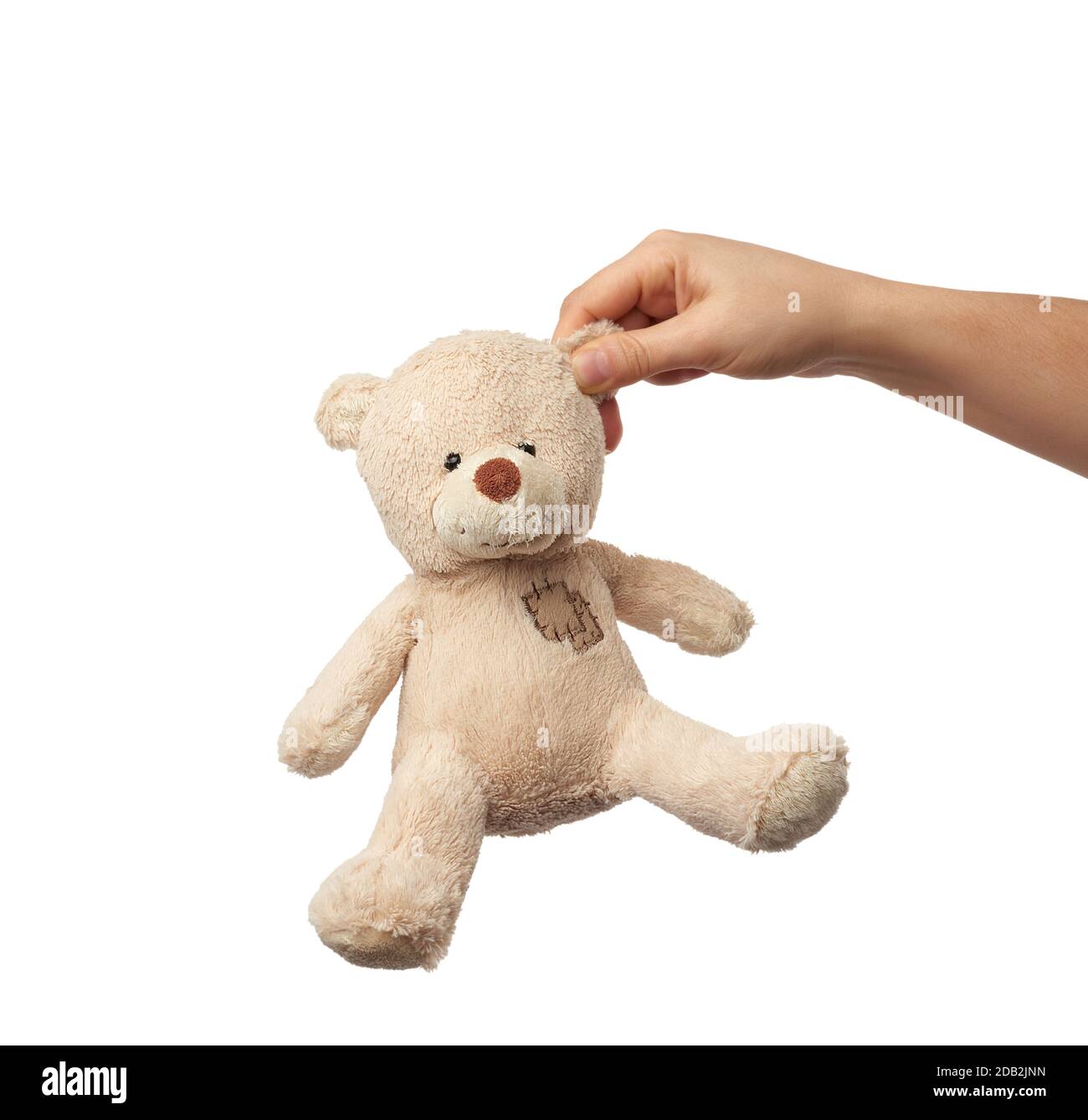 female hand holds the ear of a small beige cute teddy bear with patches ...