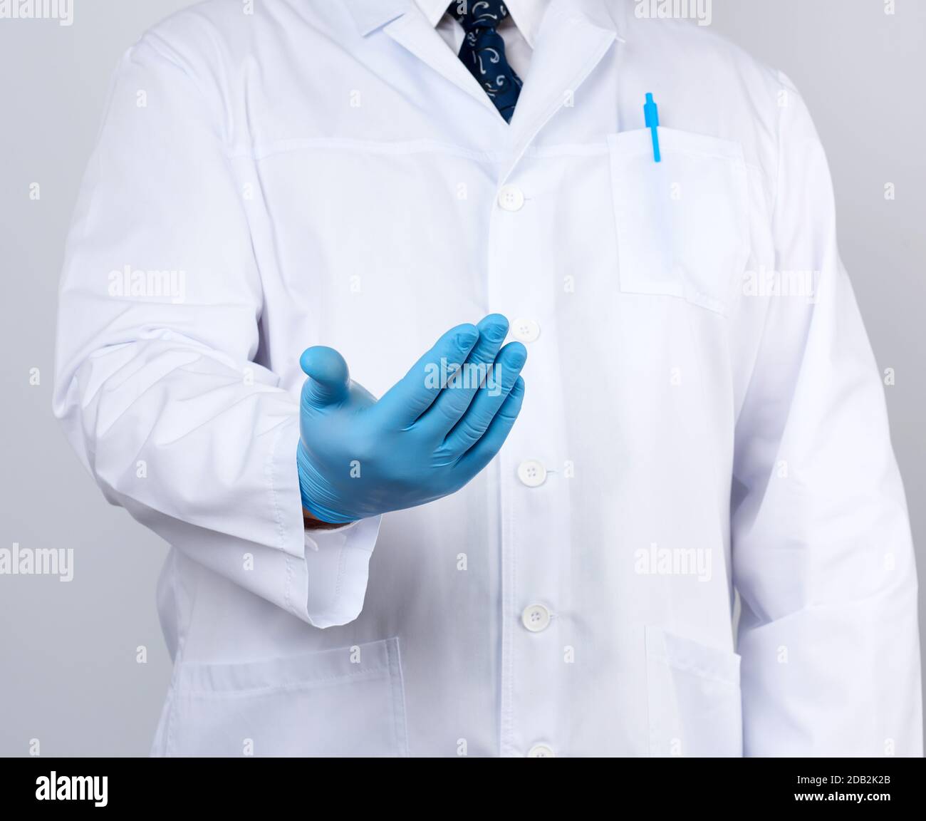 doctor in a white coat with buttons and blue latex gloves holds out his ...