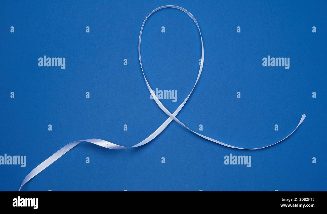 white silk thin ribbon twisted on a blue background, trendy classic ...