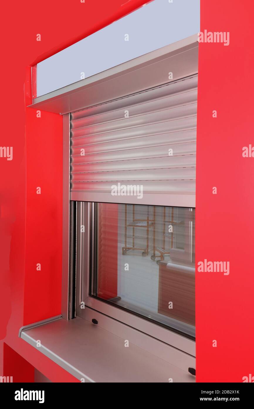 Half closed metal shutters on modern window exterior with red facade ...
