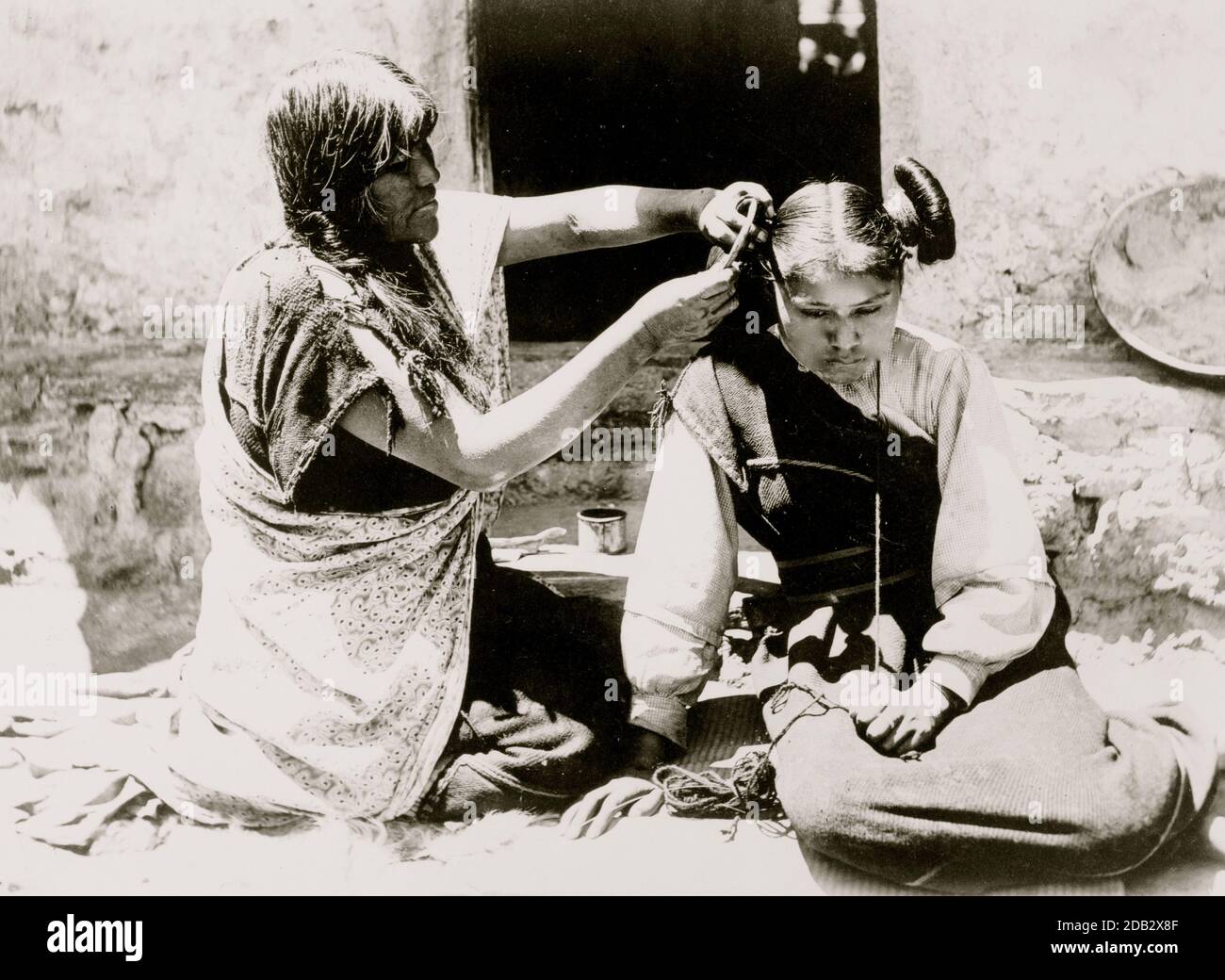 Kneeling Hopi woman combing and arranging hair of young girl Stock ...