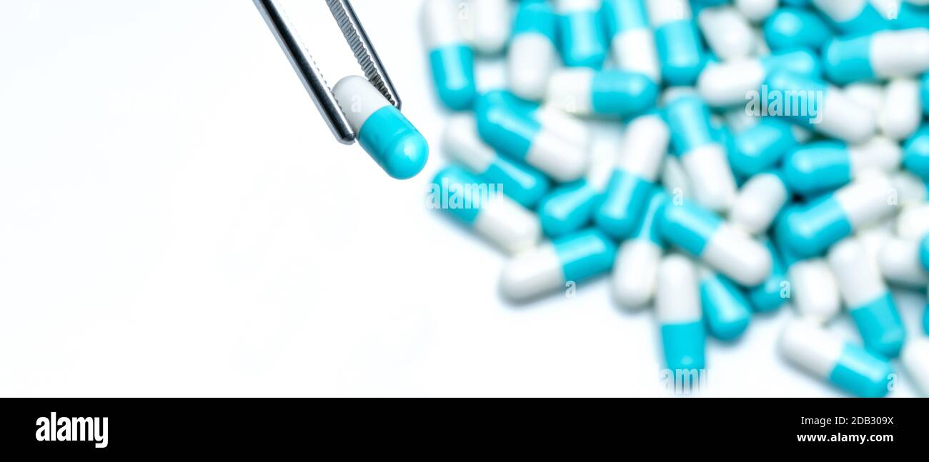 Forceps pick white-blue capsule from group of capsule pills. Drugs ...