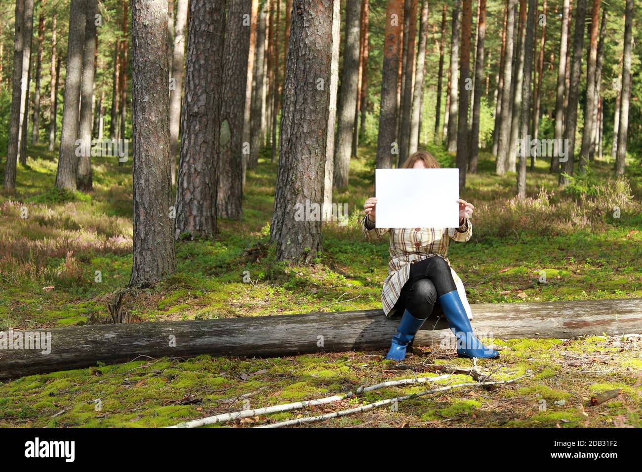 A female sitting on a tree log holding a paper with a space for text in ...