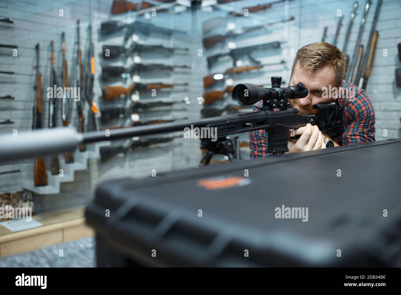 Man aims with sniper rifle in gun shop. Euqipment for hunters on stand ...