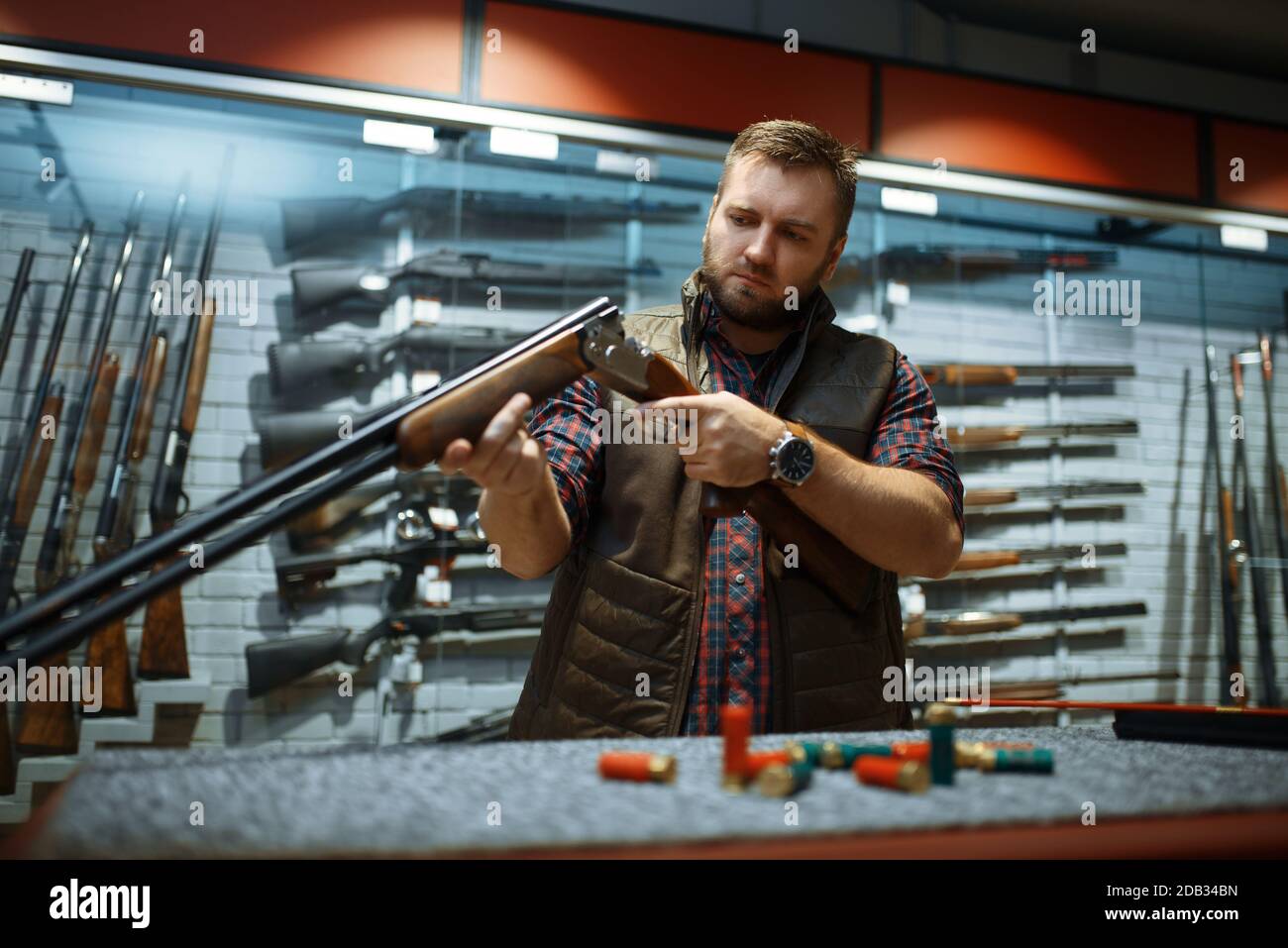 Man looks on rifle barrel at counter in gun shop. Euqipment for hunters ...
