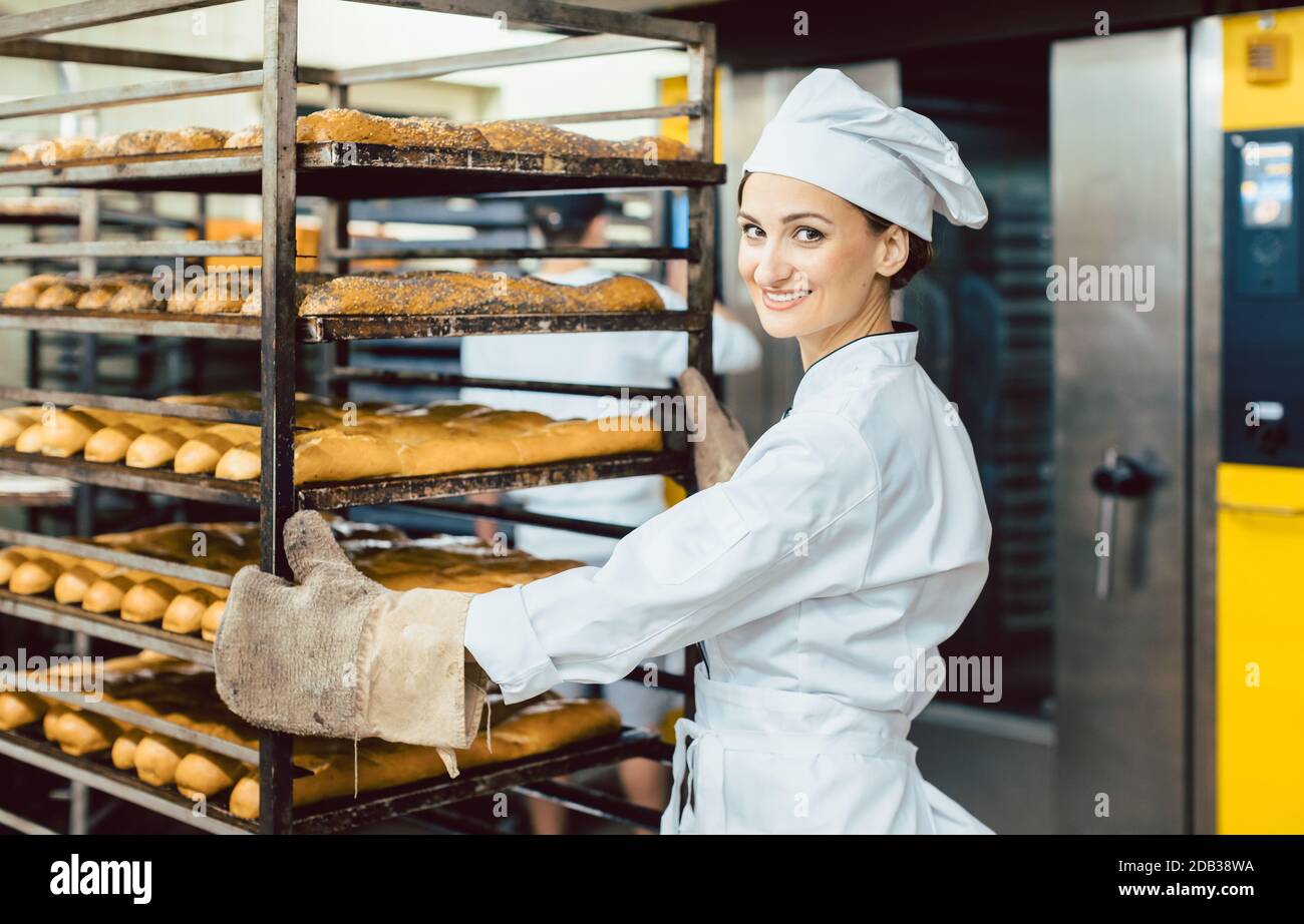 Baker woman pushing sheets with bread in the baking oven wearing bakers ...