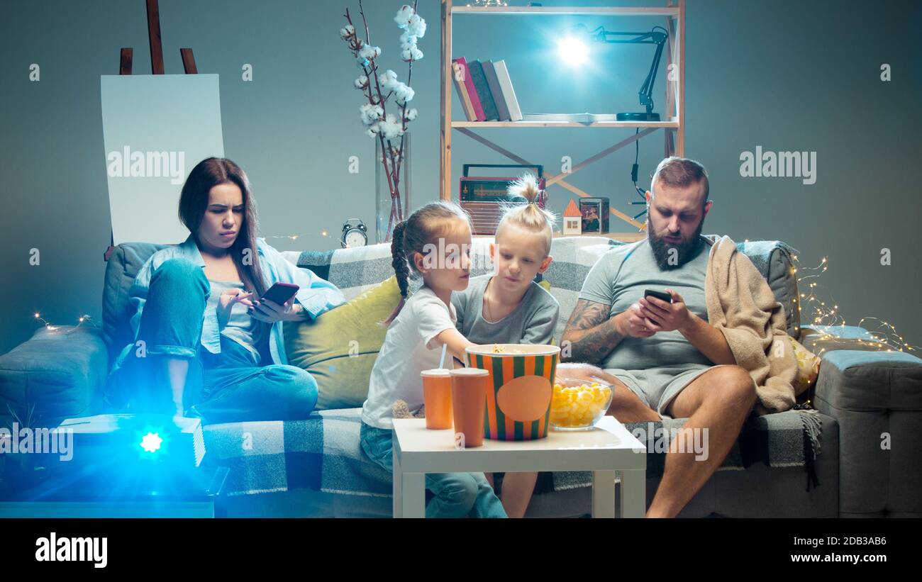 Choosing. Happy family watching projector, TV, movies with popcorn and ...
