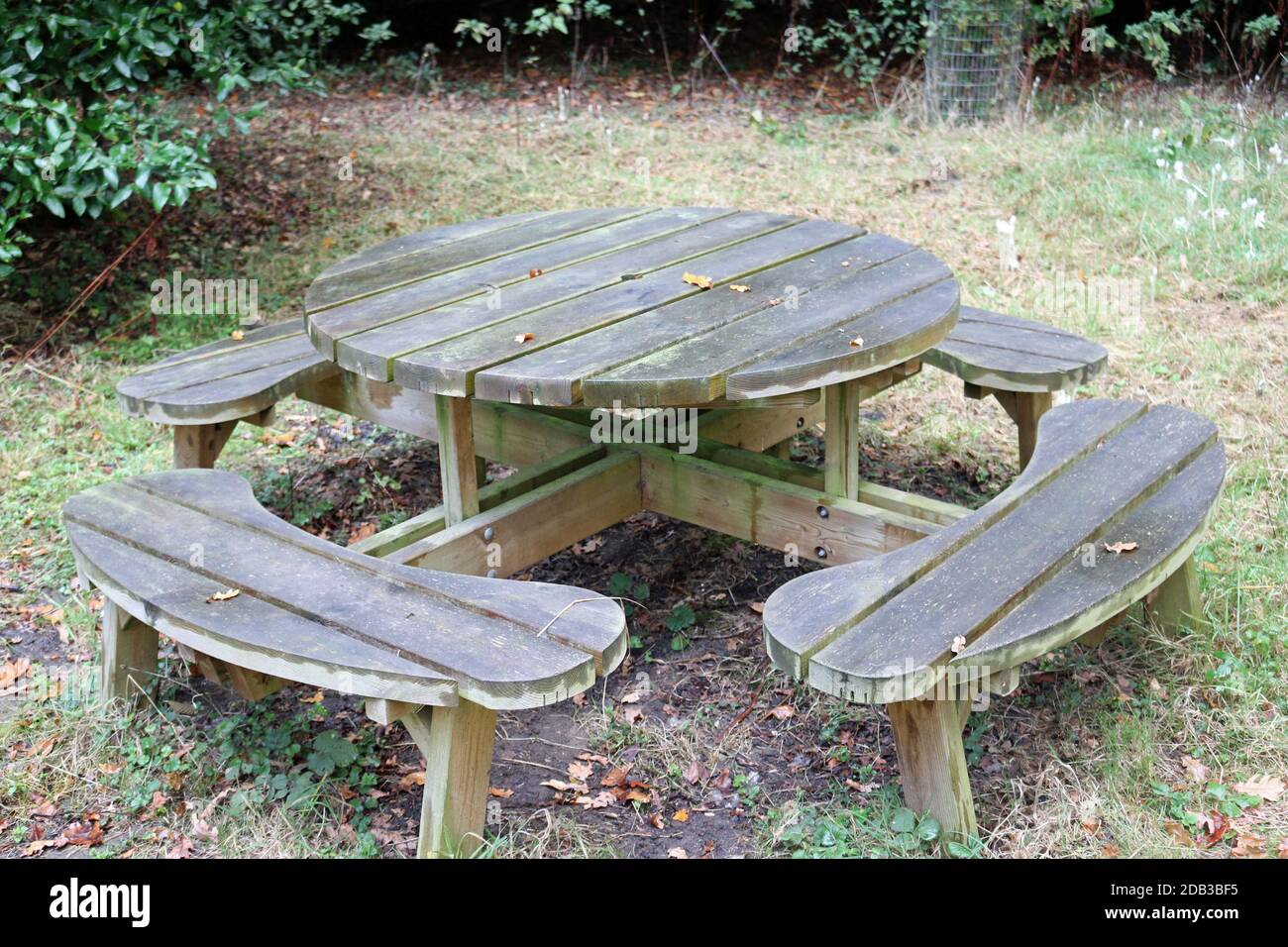 Round wooden picnic table with rounded seats on grass with soil ...