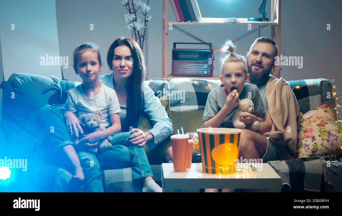 Cheerful. Happy family watching projector, TV, movies with popcorn and ...