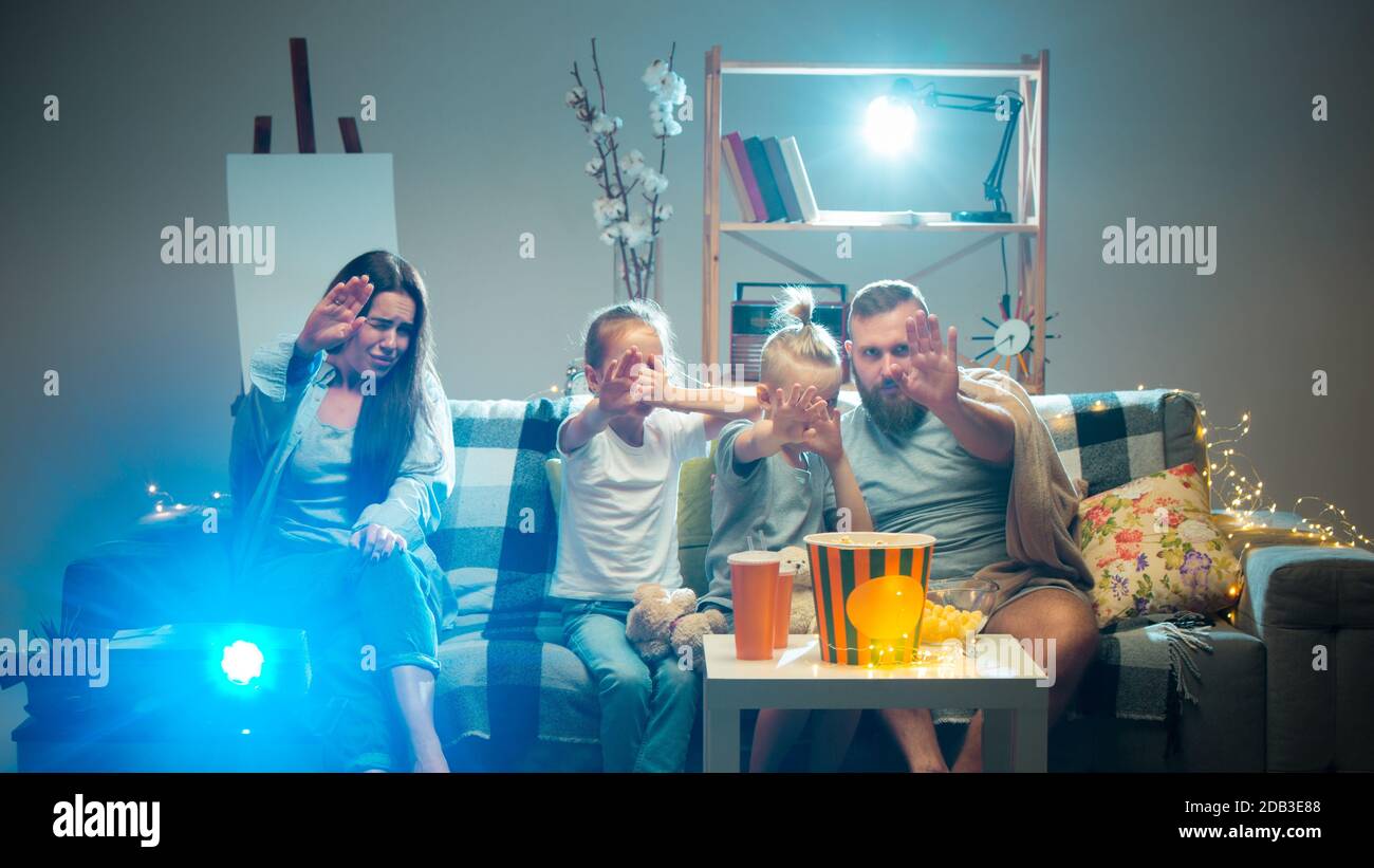 Shocked. Happy family watching projector, TV, movies with popcorn and ...