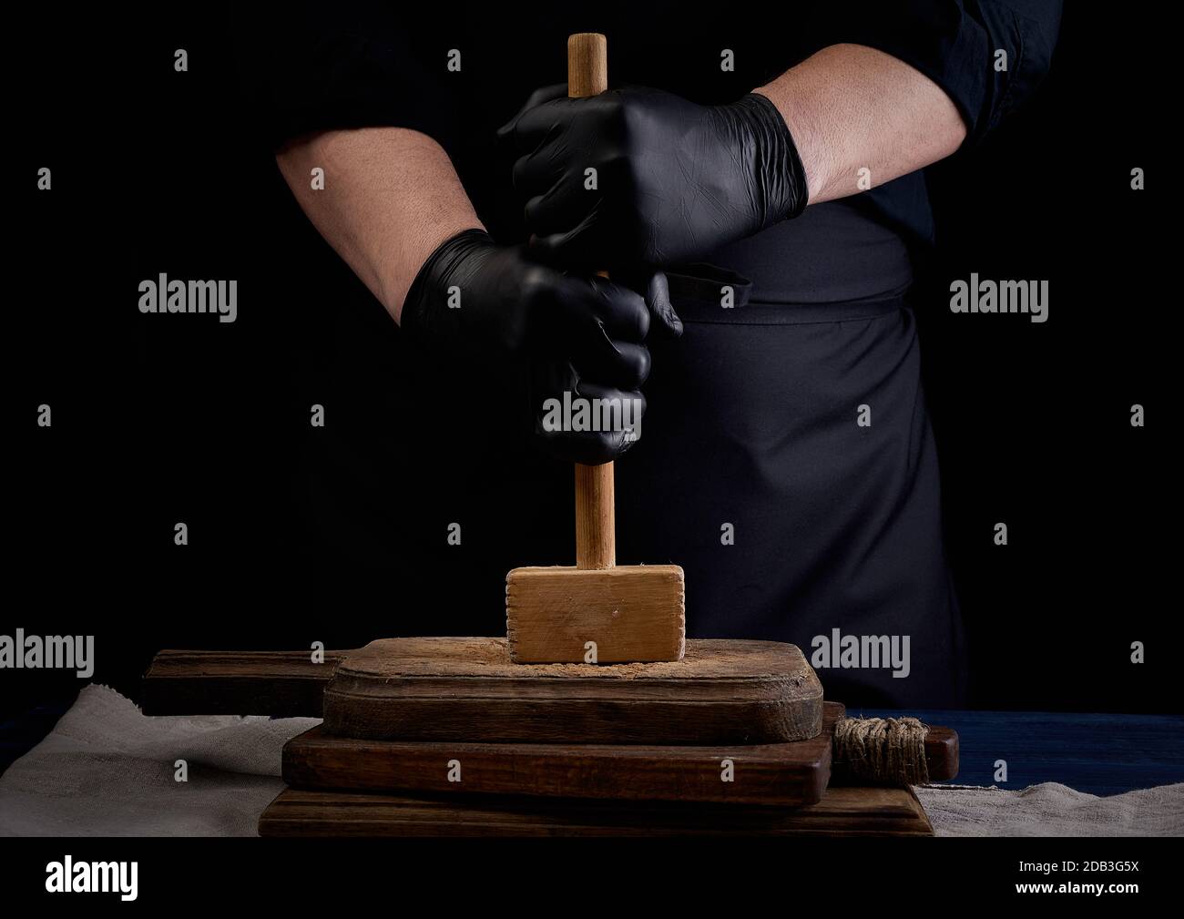 male cook in black uniform holds a wooden hammer for beating meat on a ...