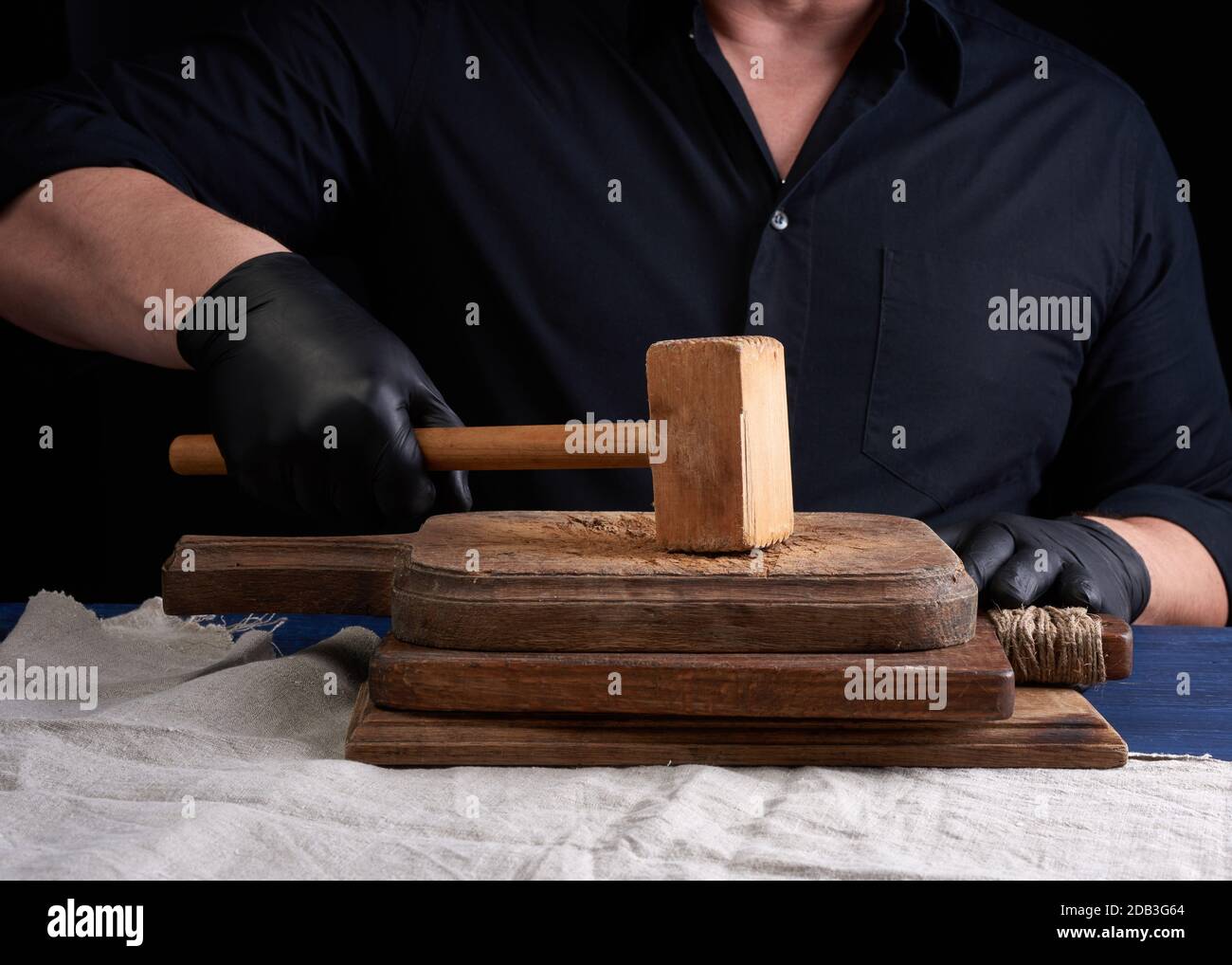 male cook in black uniform holds a wooden hammer for beating meat on a ...