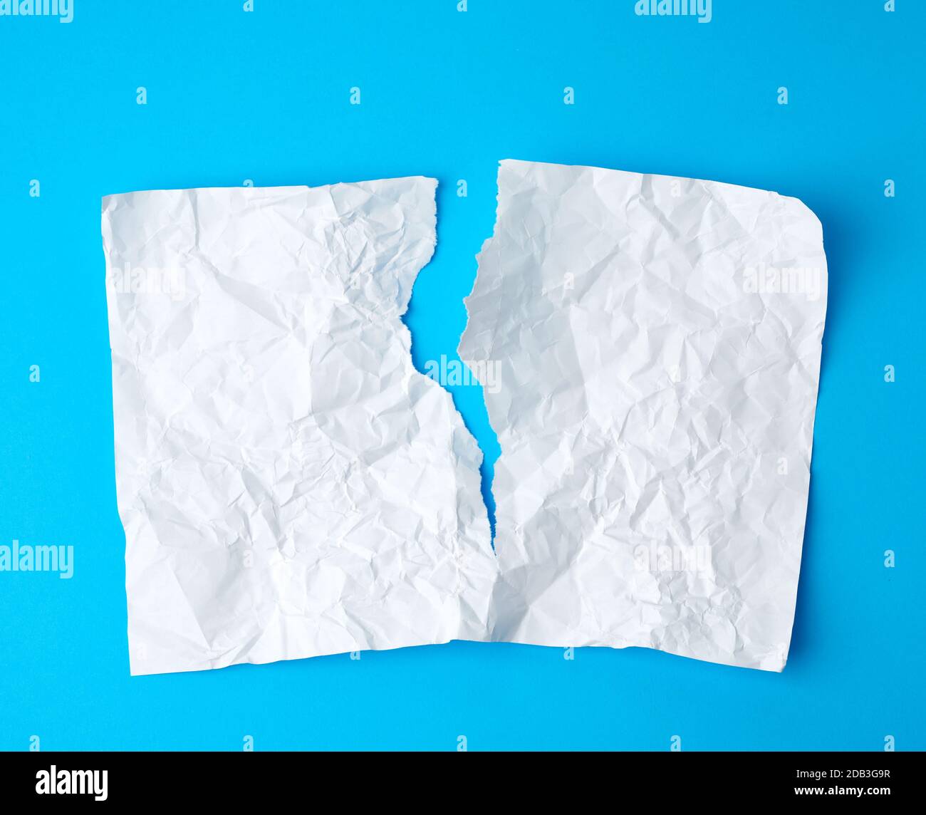 crumpled white sheet of paper torn in two on a blue background. Paper ...