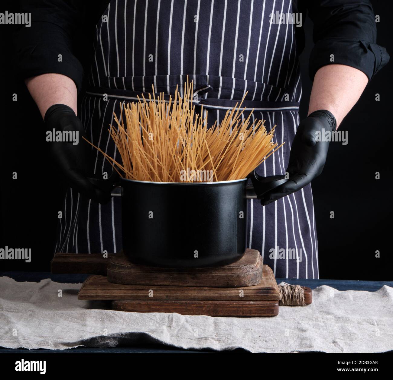 uncooked yellow long spaghetti in a black metal pan and a chef in a ...