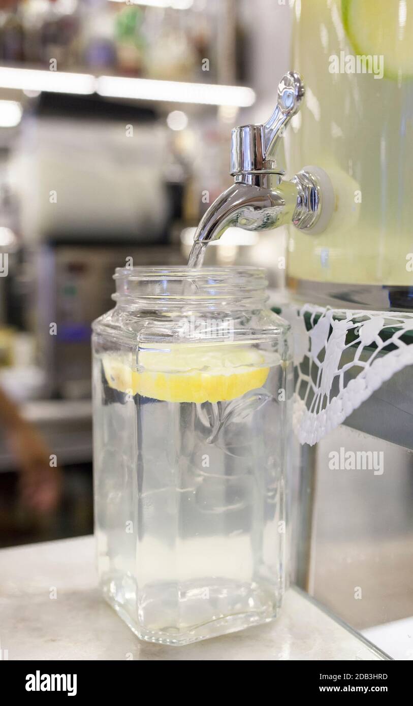 Lemonade dispenser filling a big jar with slice of lemon. Coffee shop ...