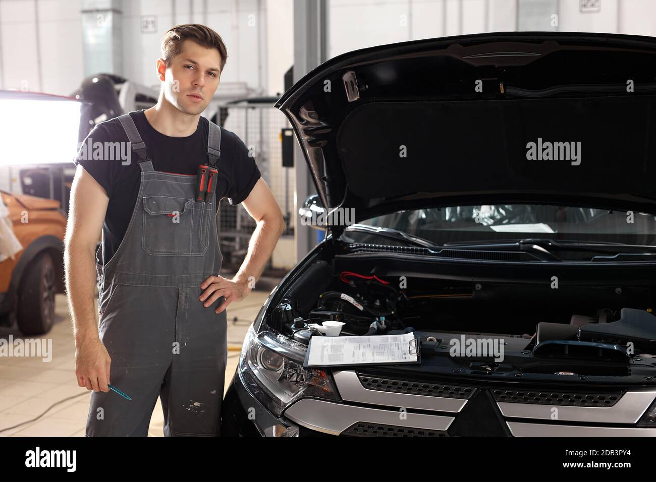 portrait of handsome caucasian auto mechanic man, standing near the car ...