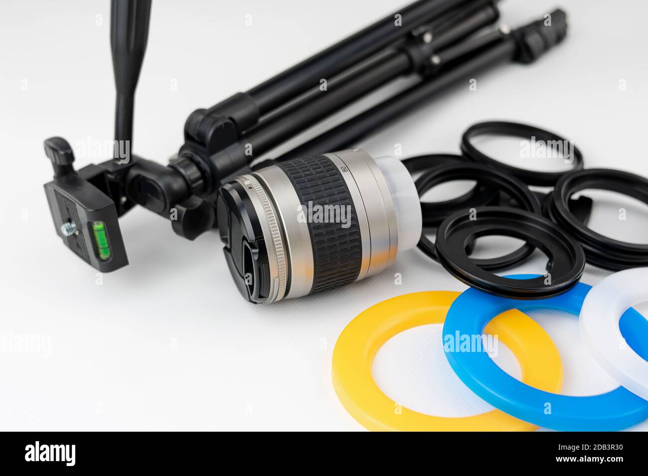 Small tripod, camera lens, color filters and adapter rings on white ...