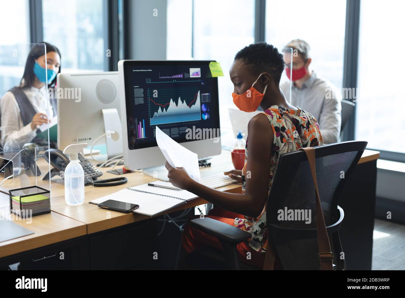 African american woman wearing face mask reading document while sitting ...