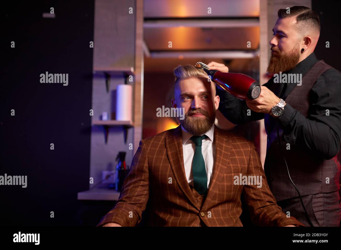 stylish man sitting in barber shop while hairdresser dry his hair ...